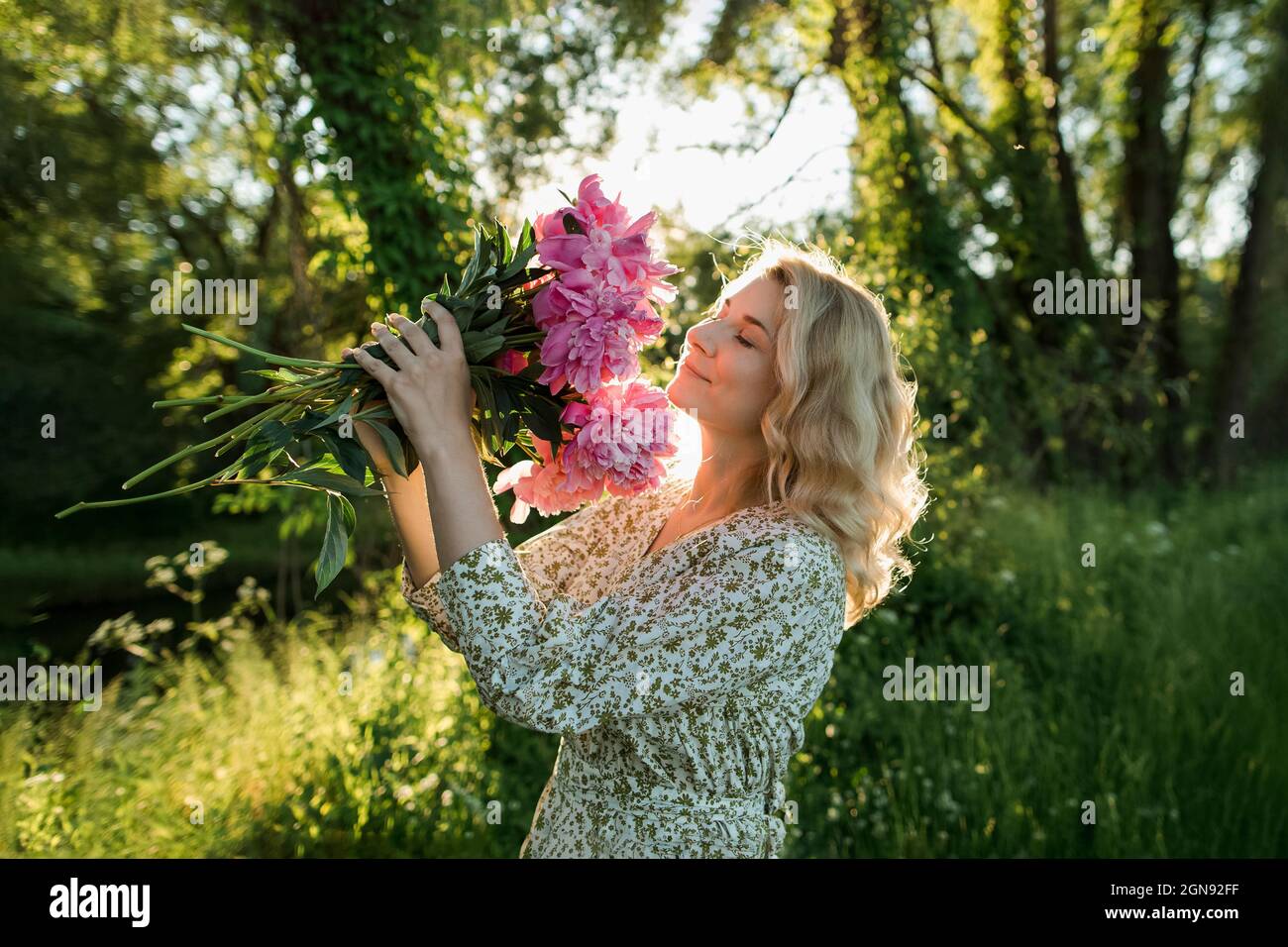 Blond woman smelling peony flower while standing at meadow Stock Photo ...
