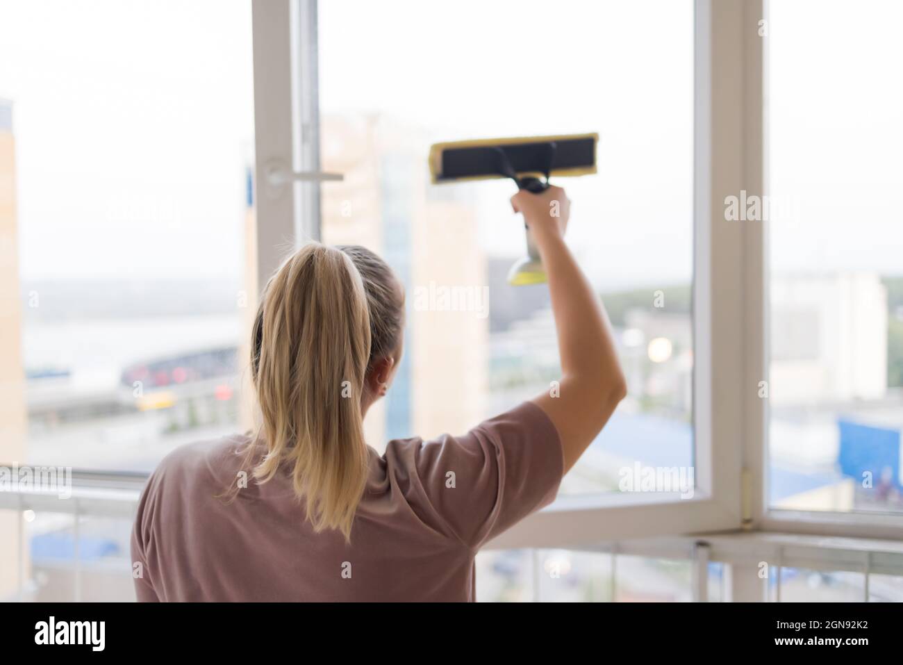 Beautiful young housewife in working clothes washing windows by ...