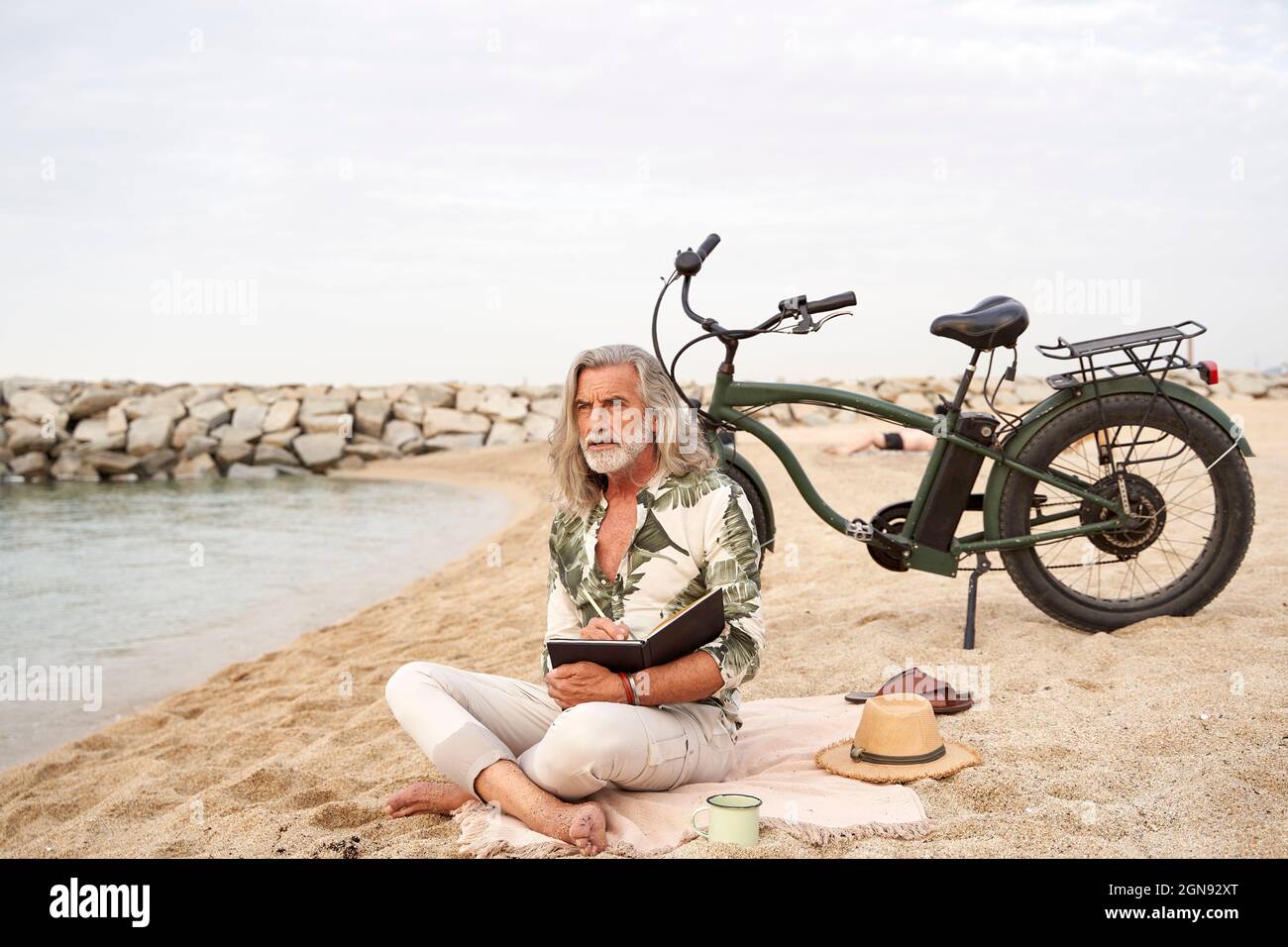 Man writing in book while sitting by bicycle at beach Stock Photo - Alamy