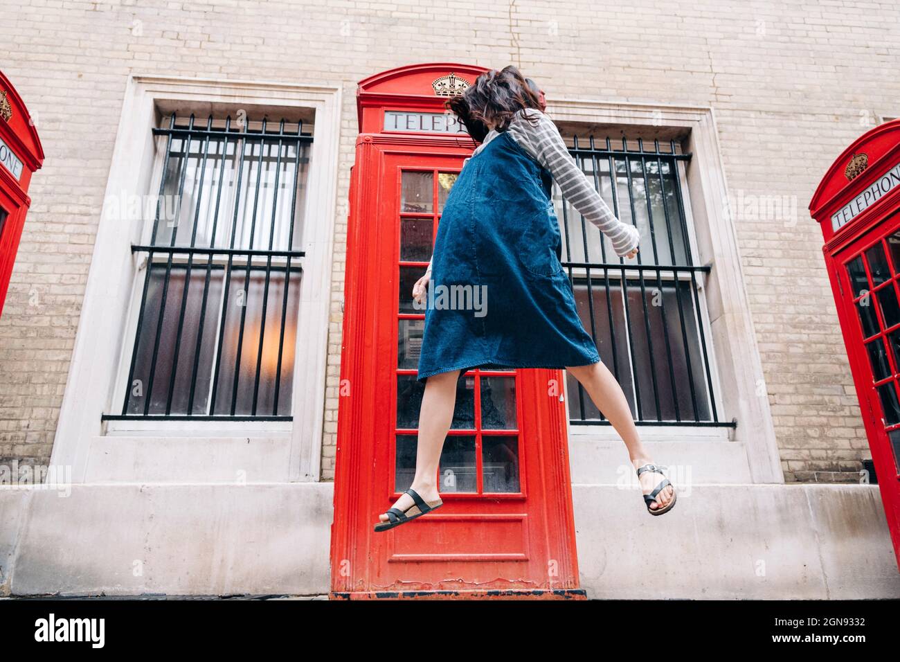 Young woman jumping in front of telephone booth Stock Photo - Alamy
