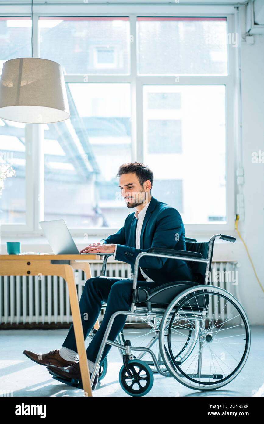 Young disabled male professional using laptop while sitting in ...