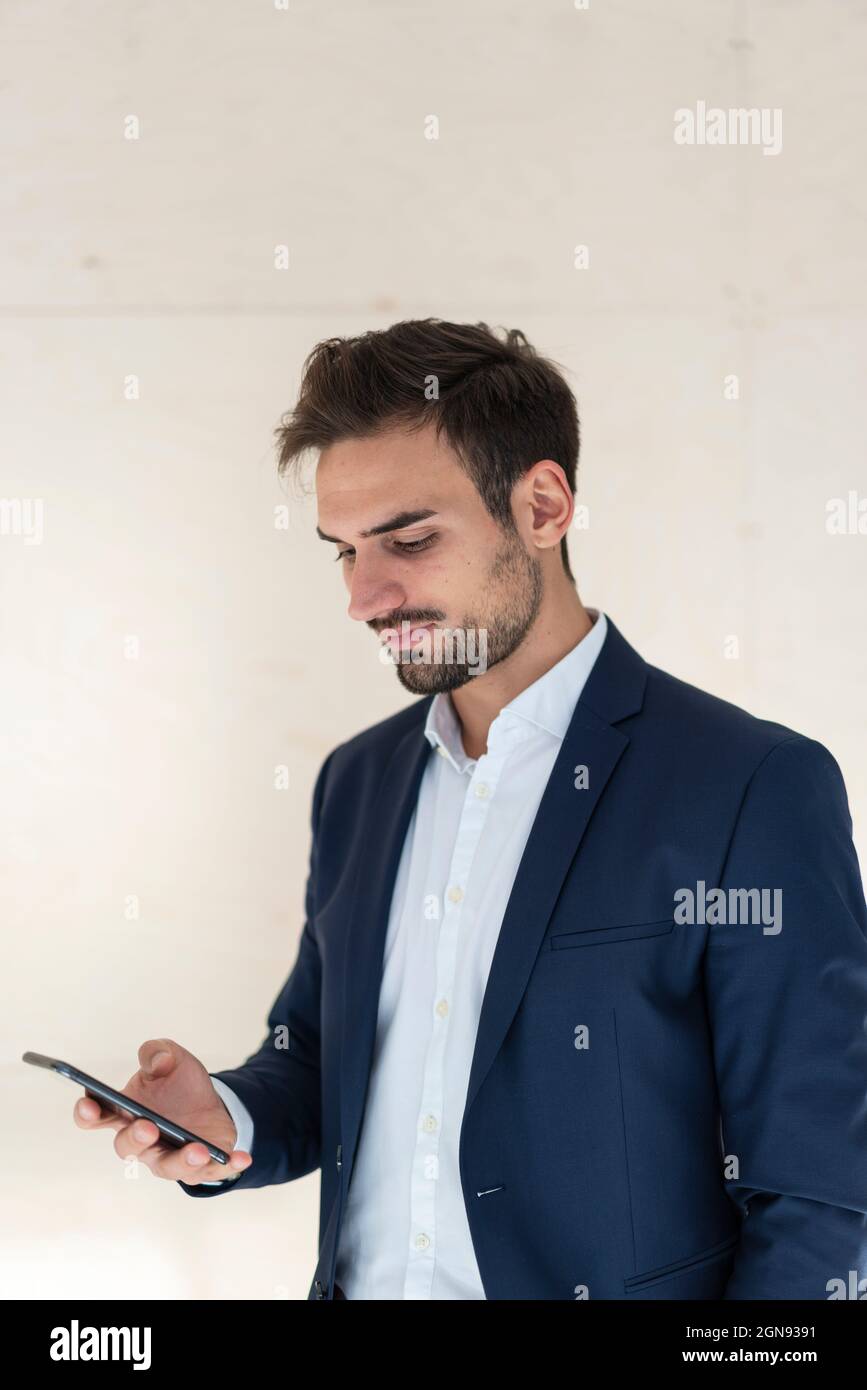 Young businessman text messaging through smart phone while standing in ...