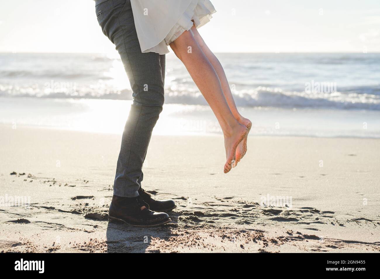 Groom picking up bride at beach during sunrise Stock Photo - Alamy