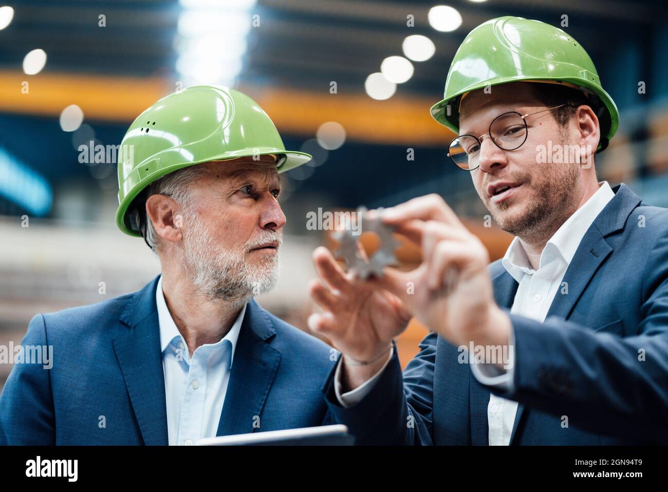 Male professional discussing over equipment with coworker in factory ...