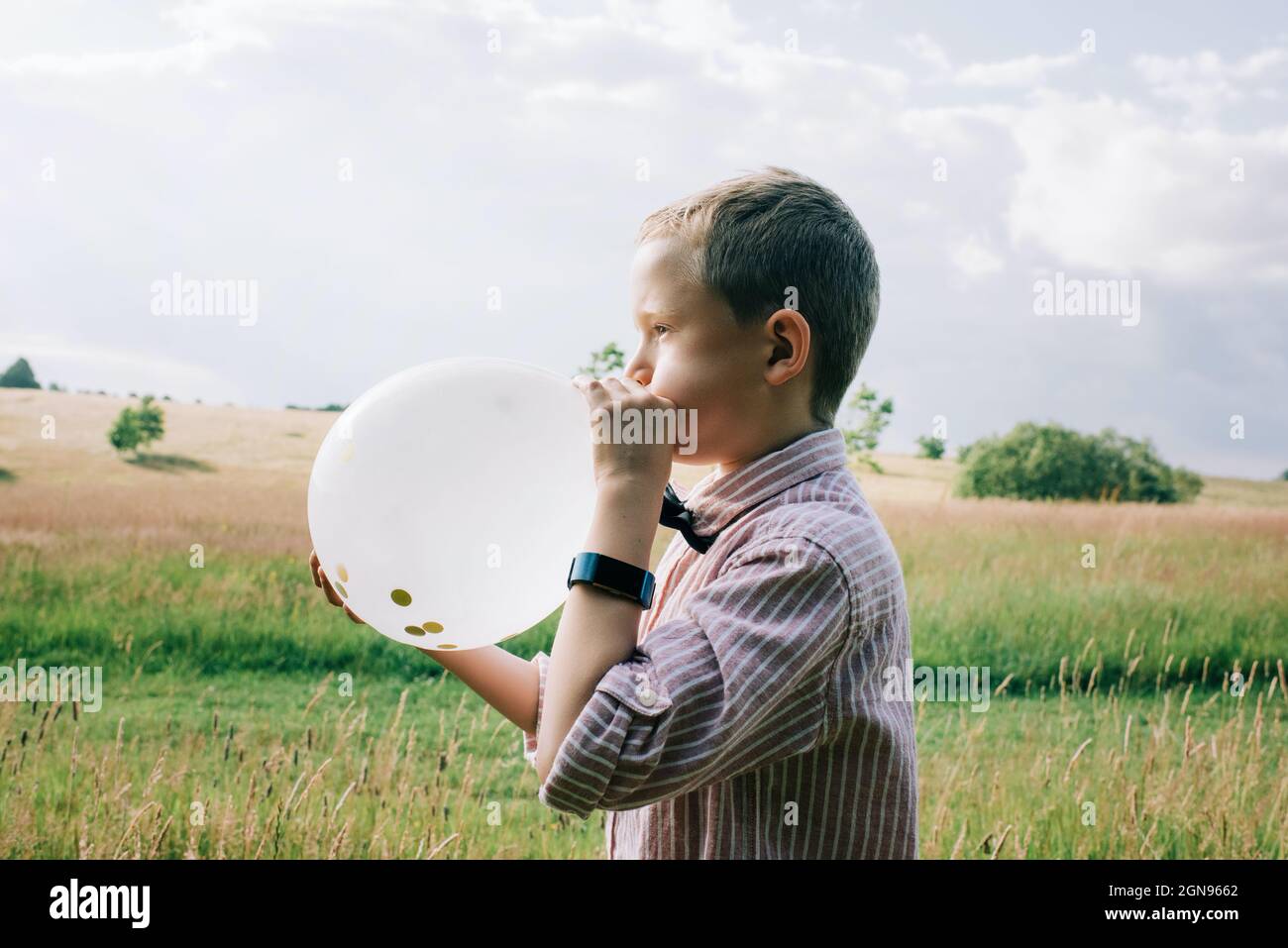 smartly dressed boy blowing up a balloon at a wedding in summer Stock ...