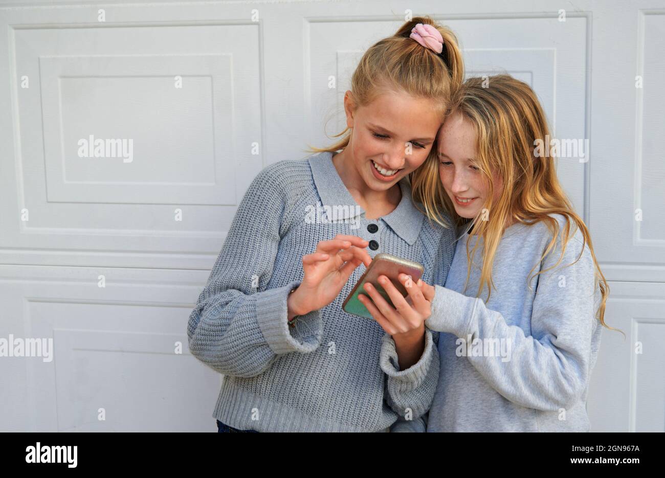 Smiling girls sharing mobile phone in front of garage door Stock Photo ...