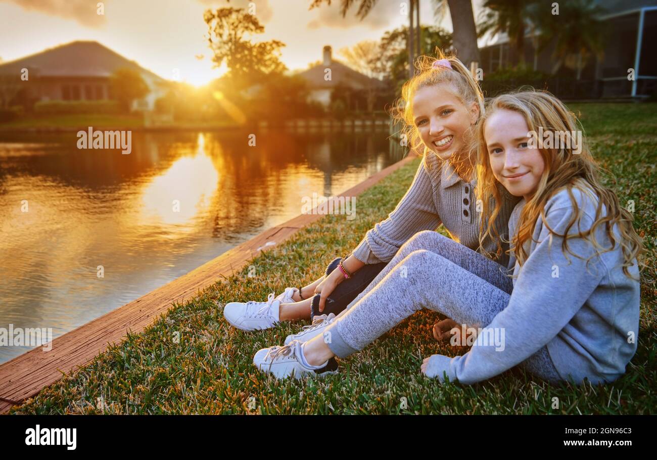 Happy girls sitting on grass by pond during sunset Stock Photo - Alamy