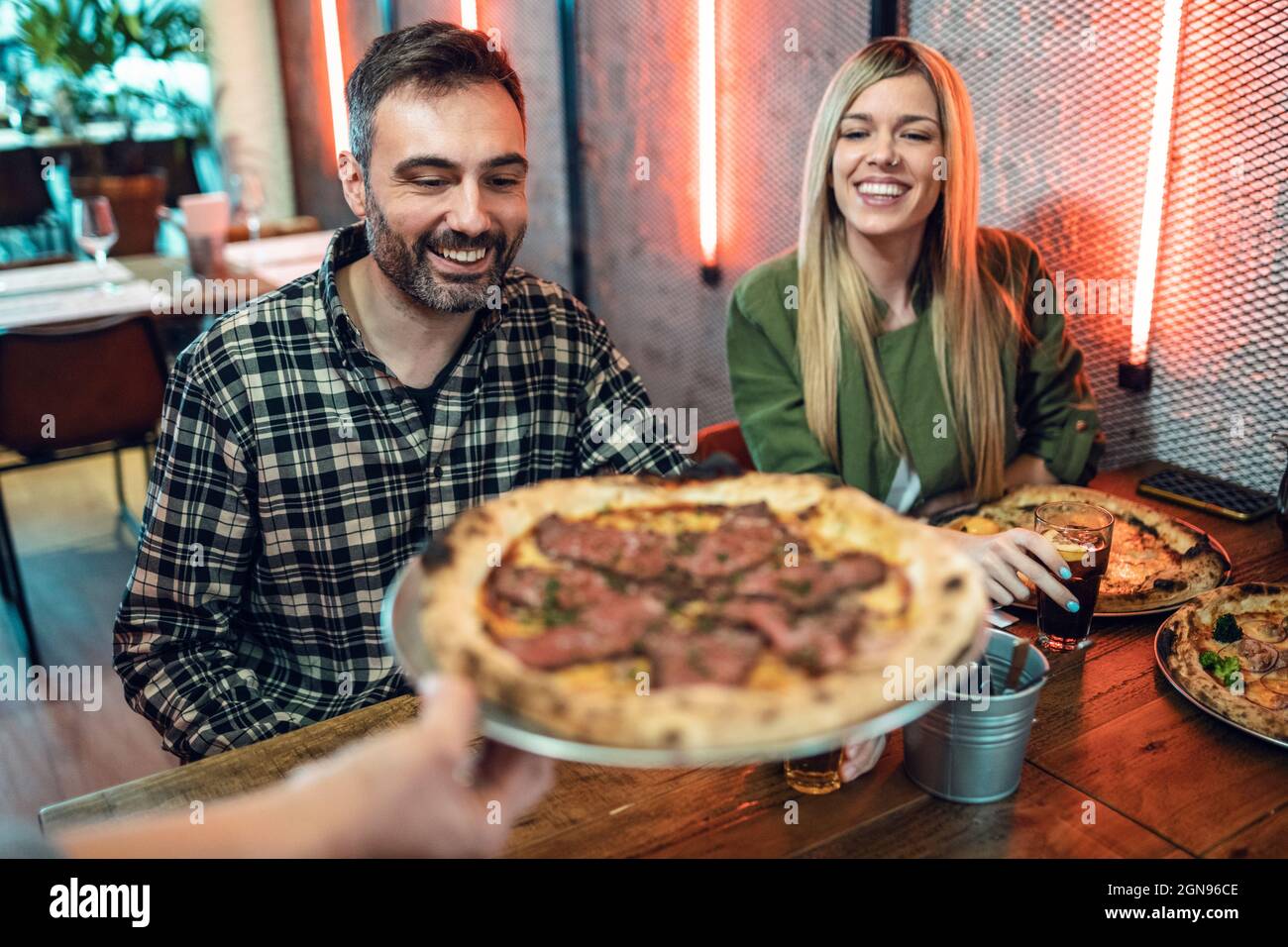 Woman offering pizza to male and female friends in restaurant Stock ...