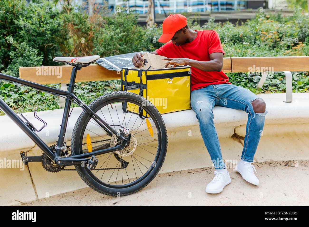 Delivery man examining package while sitting on bench Stock Photo - Alamy