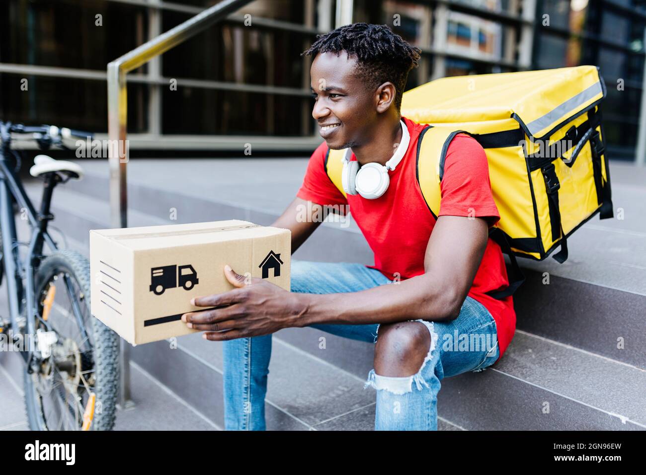 Smiling delivery man with package sitting on steps Stock Photo - Alamy