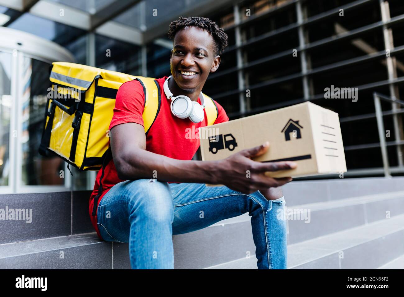 Happy delivery man holding box while sitting on steps Stock Photo - Alamy