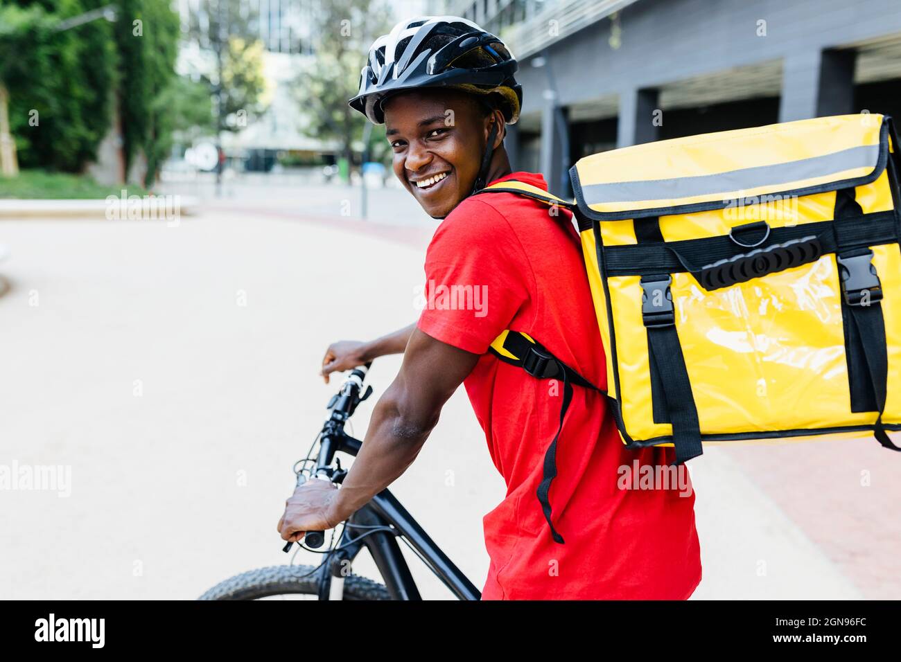 Happy young delivery man wearing backpack sitting on bicycle Stock ...