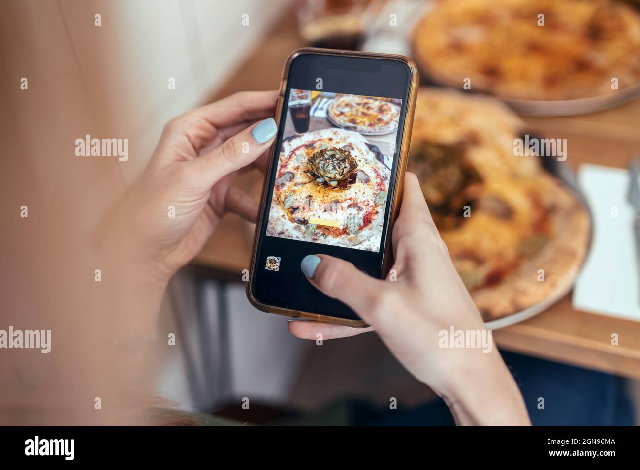 Mid adult woman photographing pizza through smart phone in restaurant ...