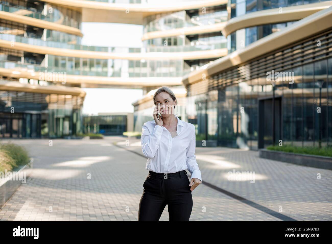 Smiling female professional talking on smart phone outside office ...