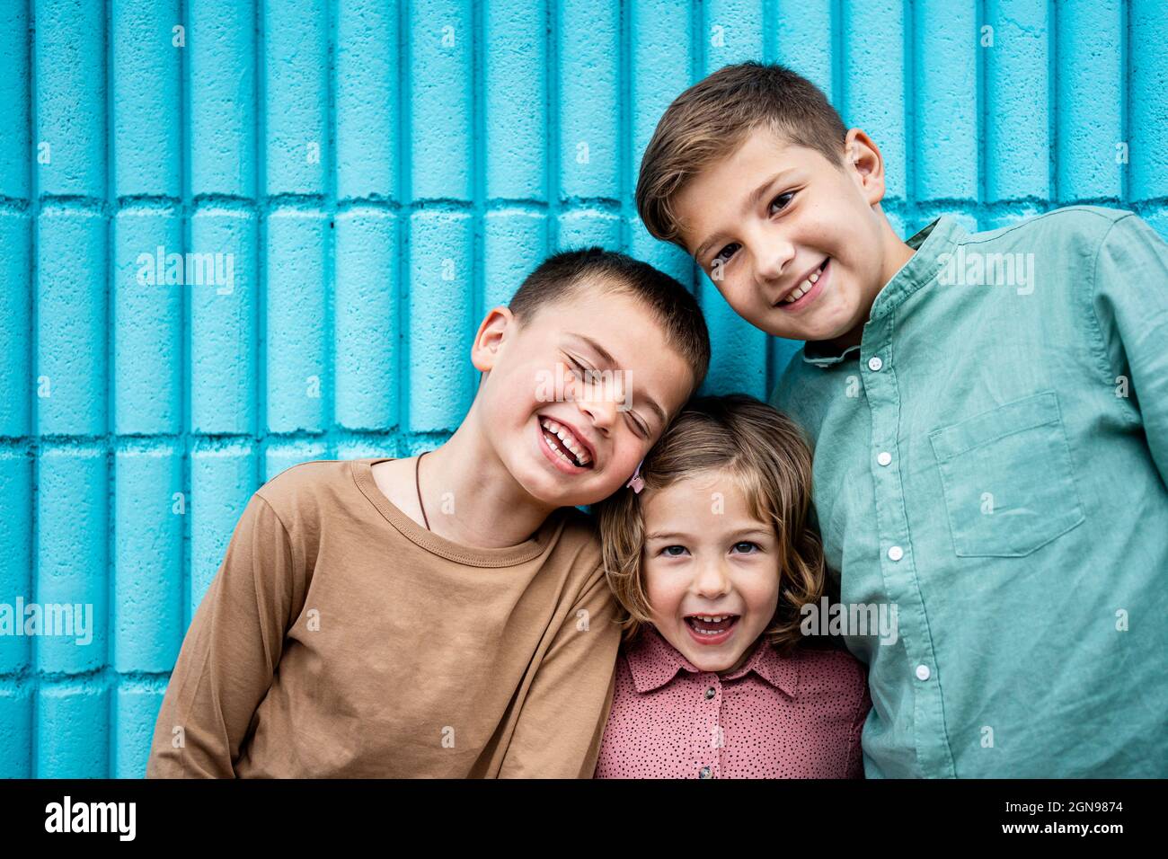 Happy girl and boys standing together in front of blue wall Stock Photo ...