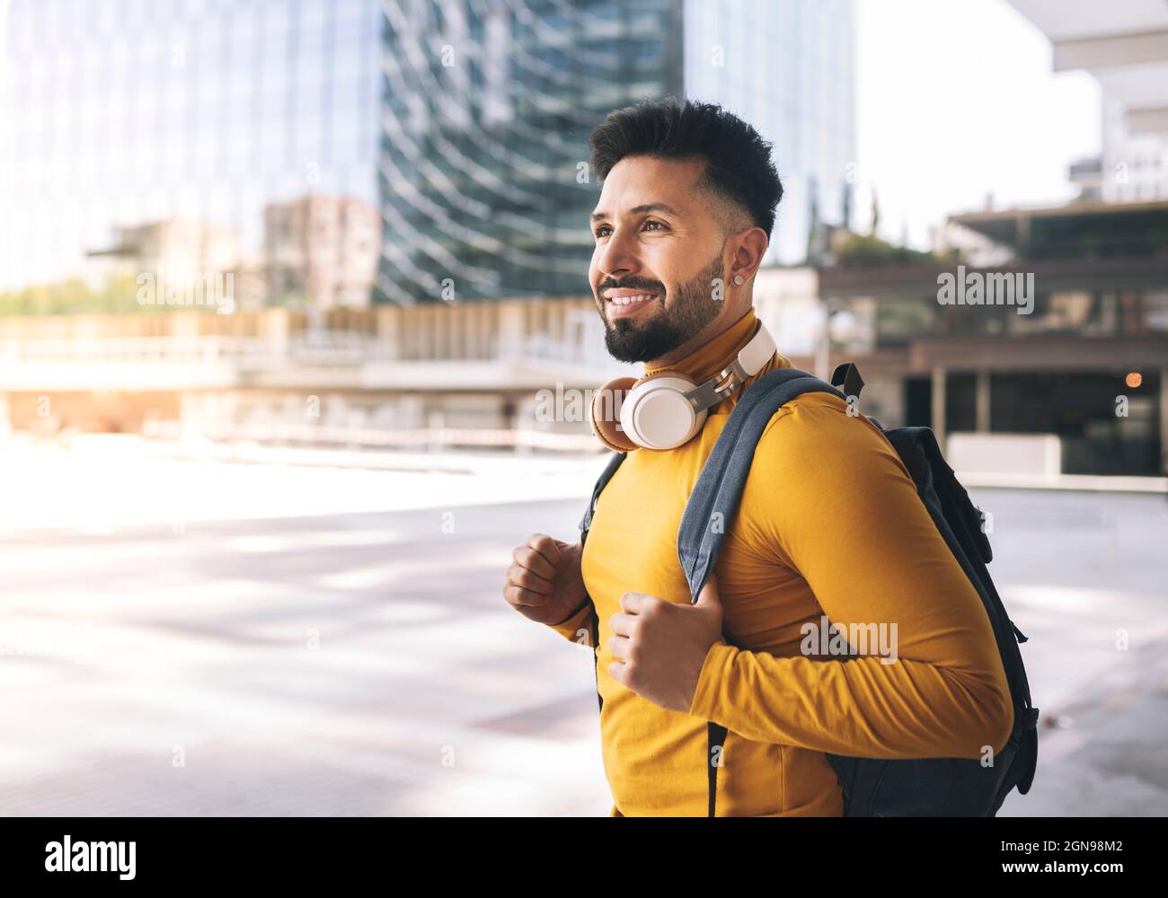 Man with headphones and backpack standing by glass wall Stock Photo - Alamy