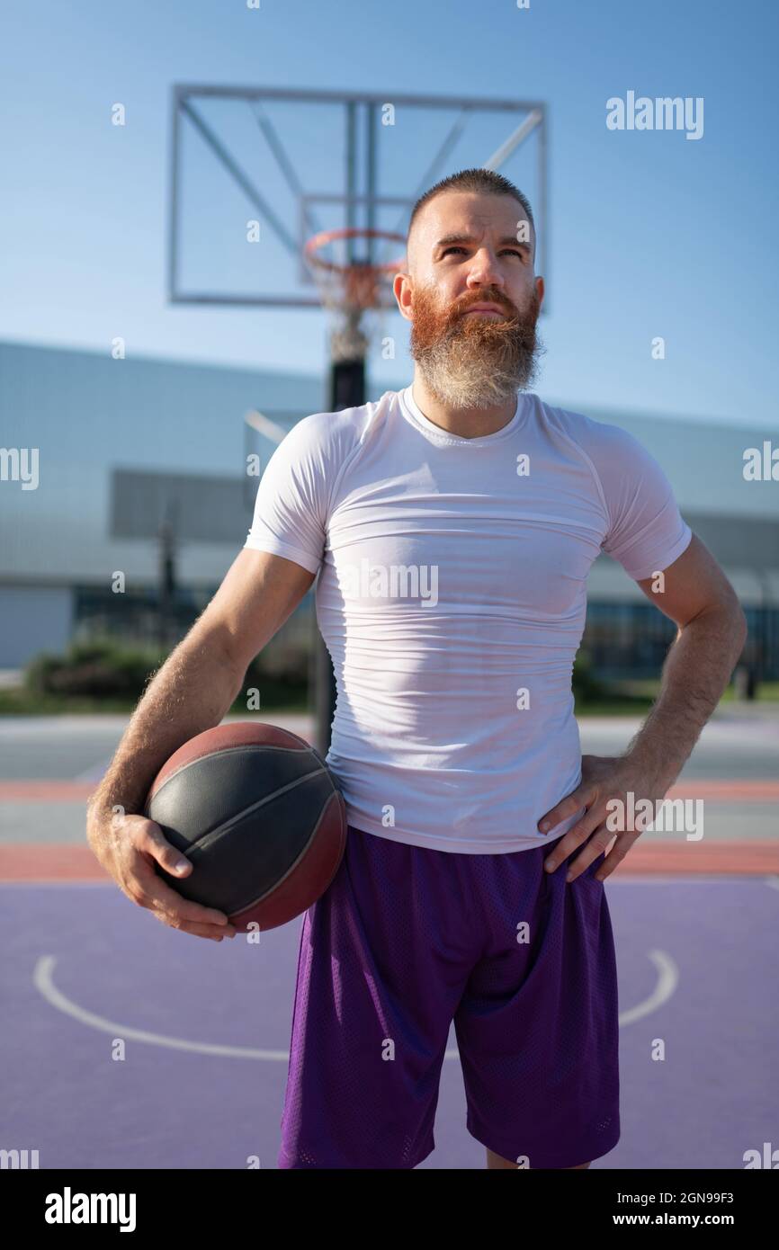 Self assured basketball player with ball holding hand on waist during ...