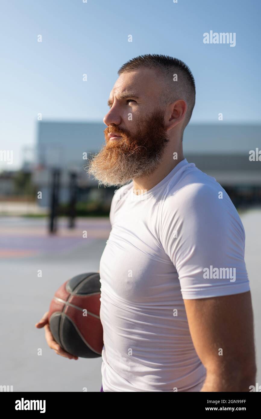 Serious bearded sportsman with ball standing on basketball court in ...
