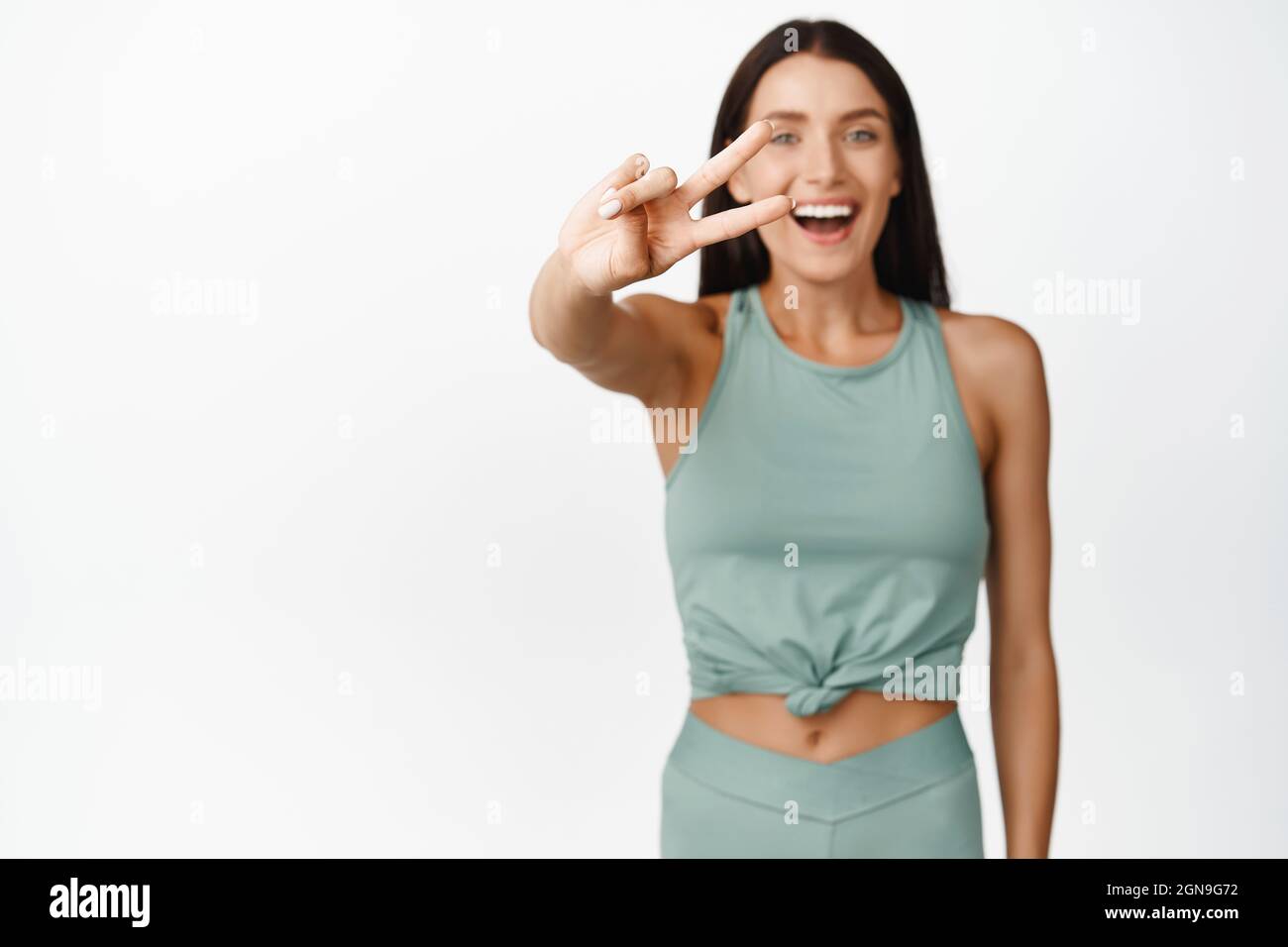 Happy laughing fitness girl shows vsign and smiling, standing in ...
