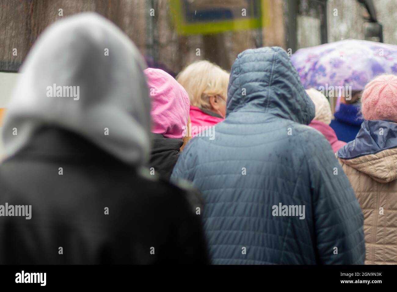 People from the back in the rain. Hooded people walk towards the bus ...