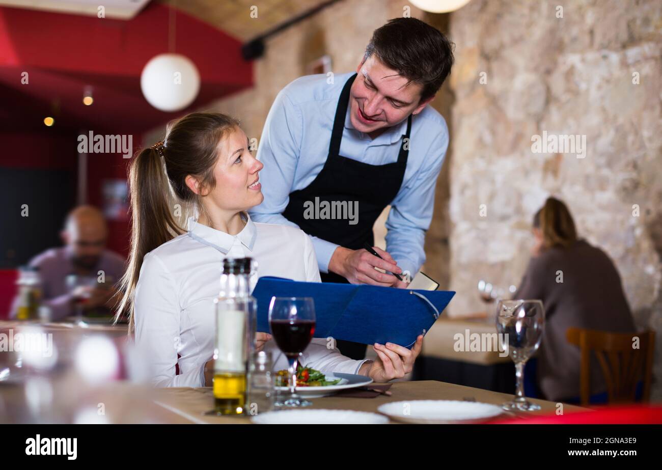 Hospitable waiter helping adult girl with menu Stock Photo - Alamy