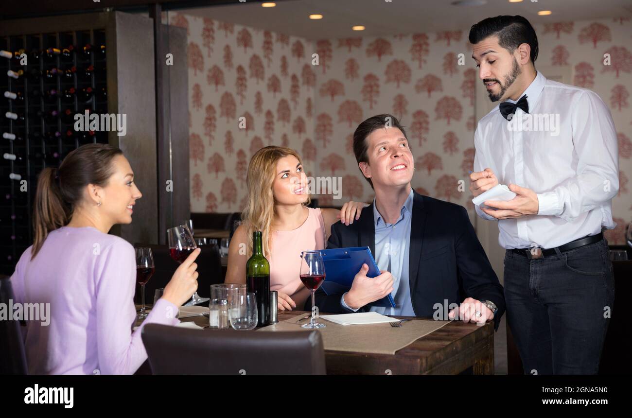 Handsome waiter taking order from young people in restaurant Stock ...