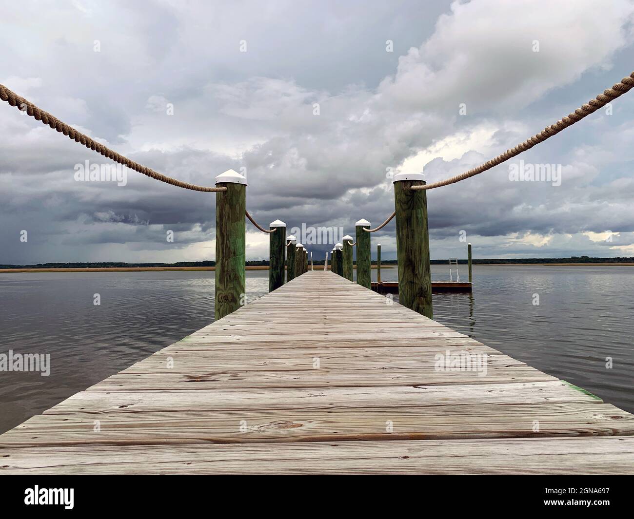 Wooden dock with ropes on stormy cloudy day over water on salt marsh ...