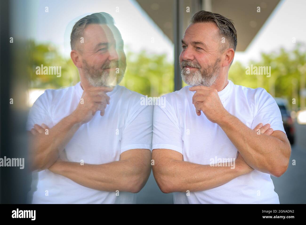 Playful man leaning against a window looking at his own reflection in ...