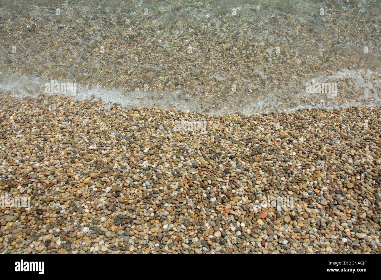 Small pebbles on the shore in a beach with wavy sea. Summer background ...