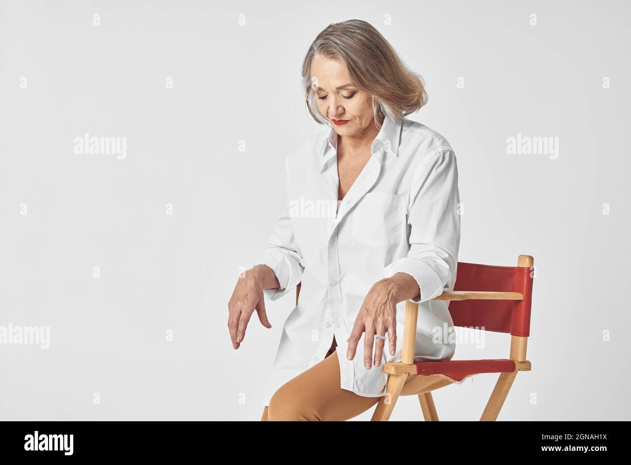 aged woman in white shirt sits on a chair red lips isolated background ...