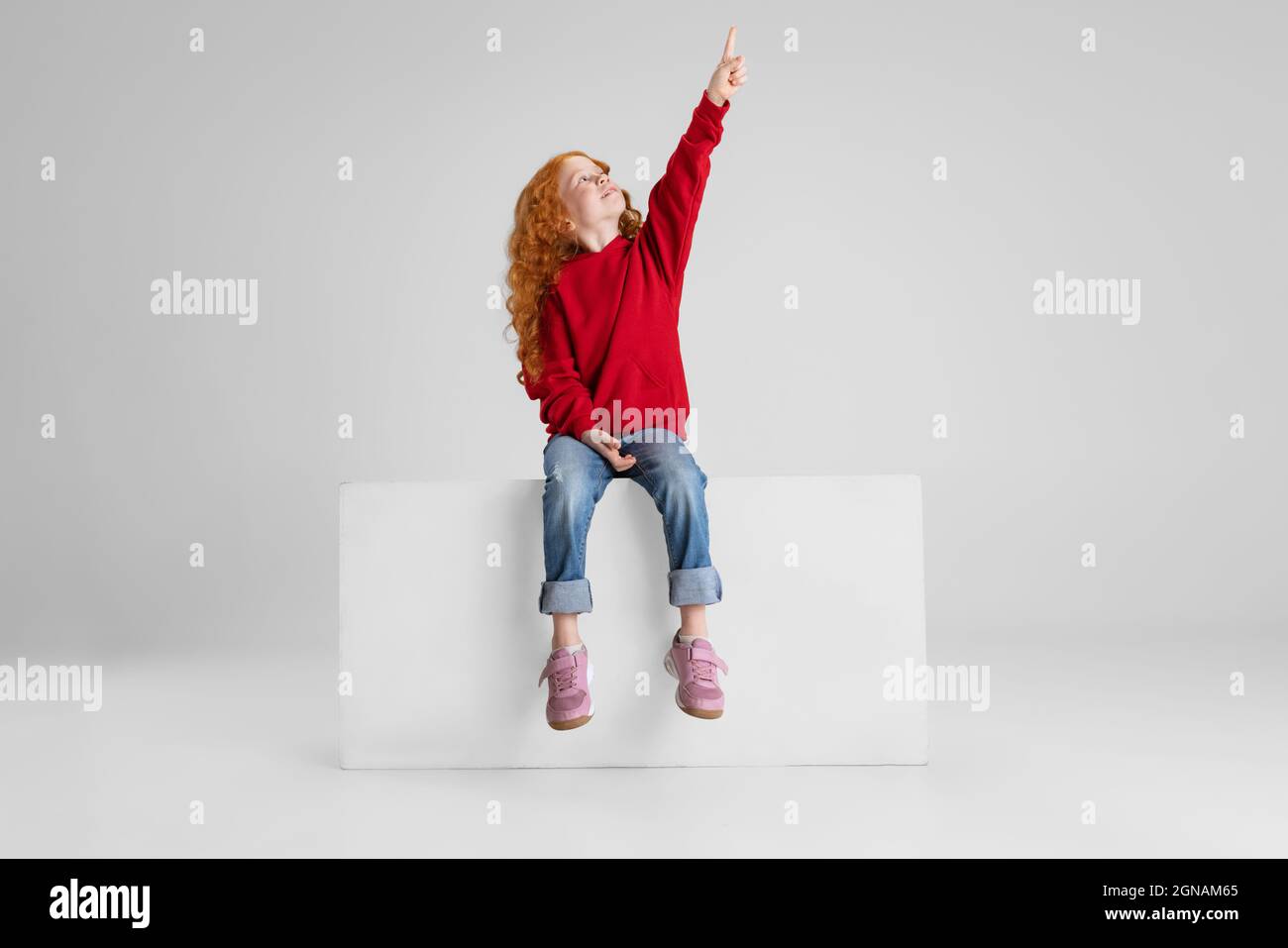 Portrait of little red-haired curly girl, child pointing somewhere ...