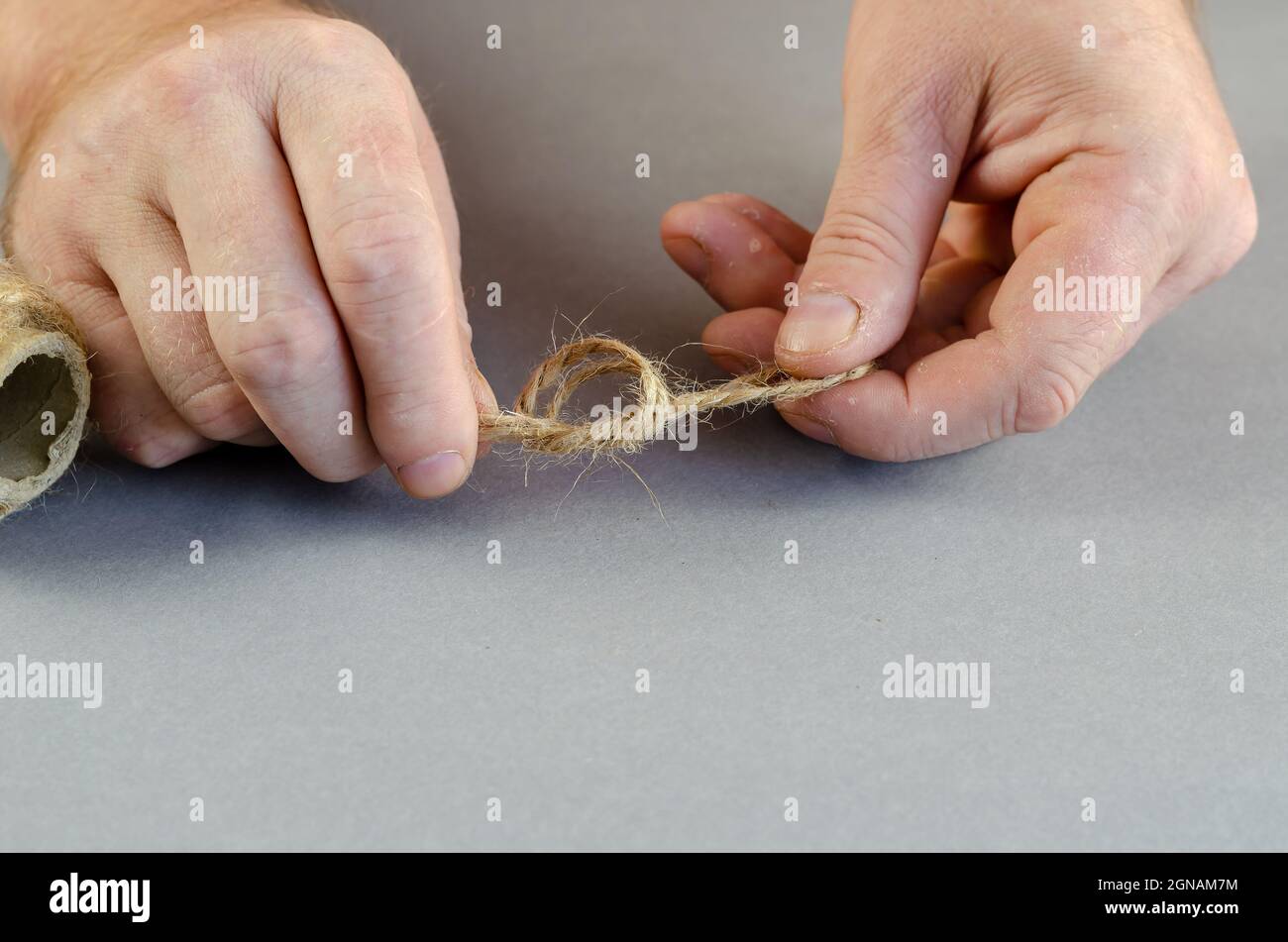 An adult male ties a knot of twine on a gray background. Hands h Stock ...