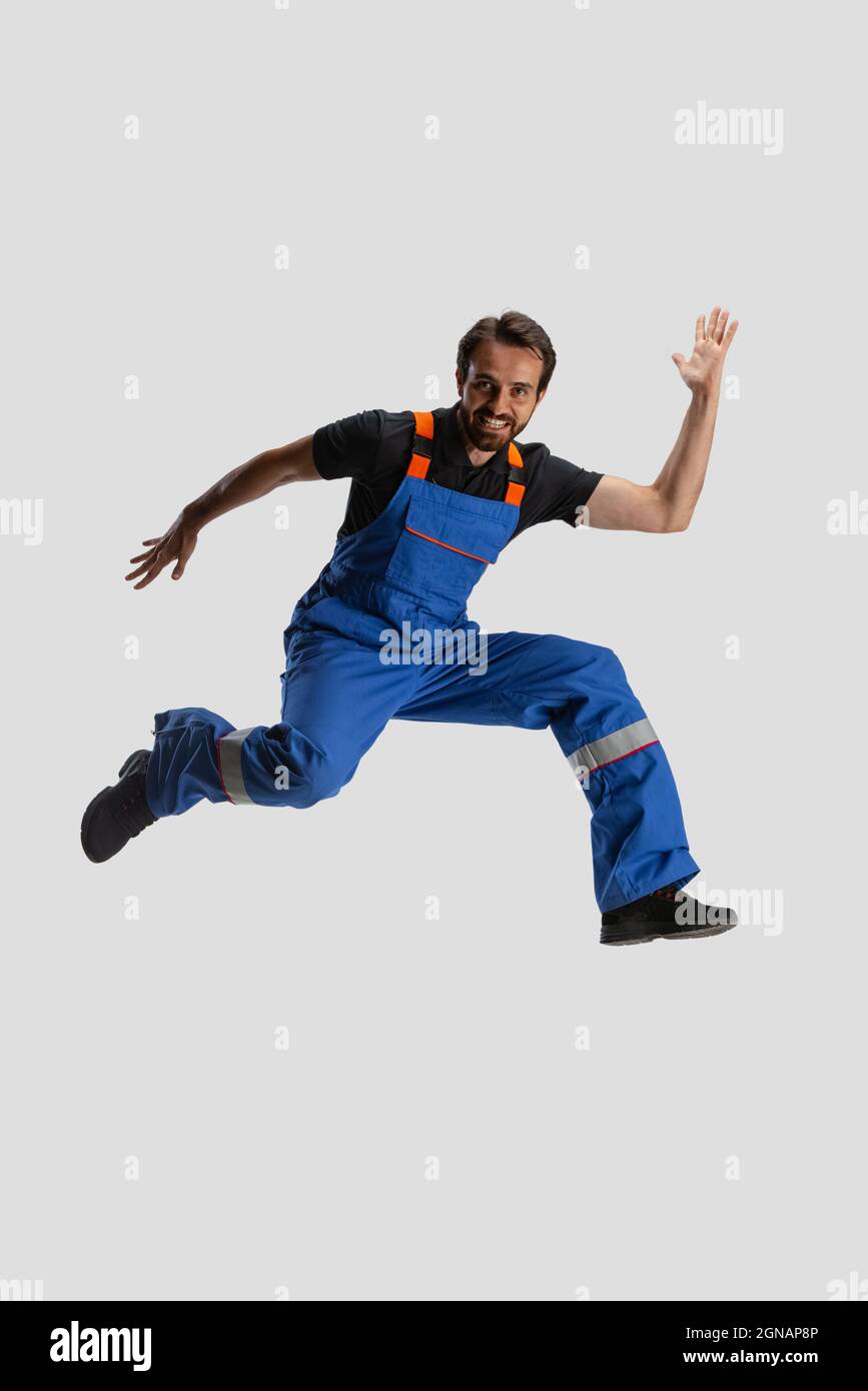 Comic portrait of young man, male auto mechanic in dungarees jumping ...