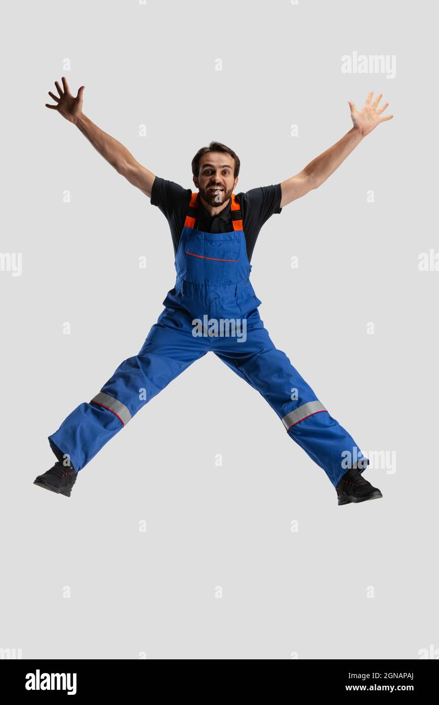 Comic portrait of young man, male auto mechanic in dungarees jumping ...