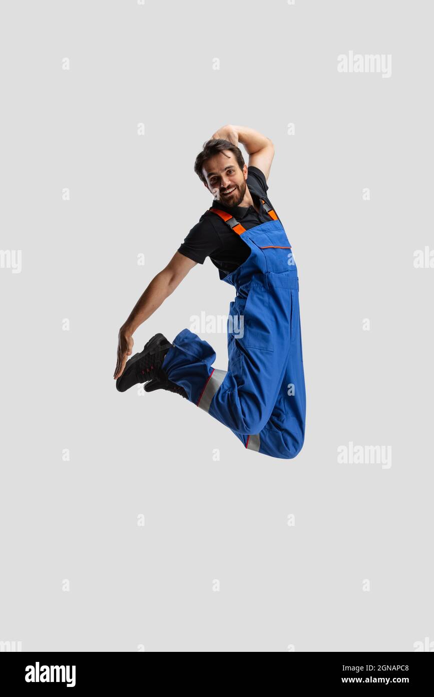 Comic portrait of young man, male auto mechanic in dungarees jumping ...