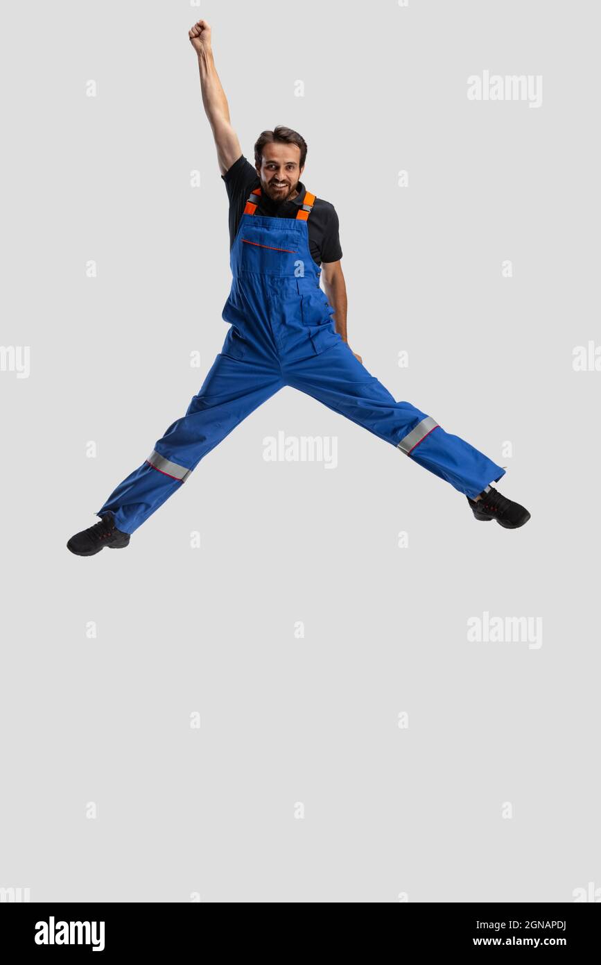 Comic portrait of young man, male auto mechanic in dungarees jumping ...