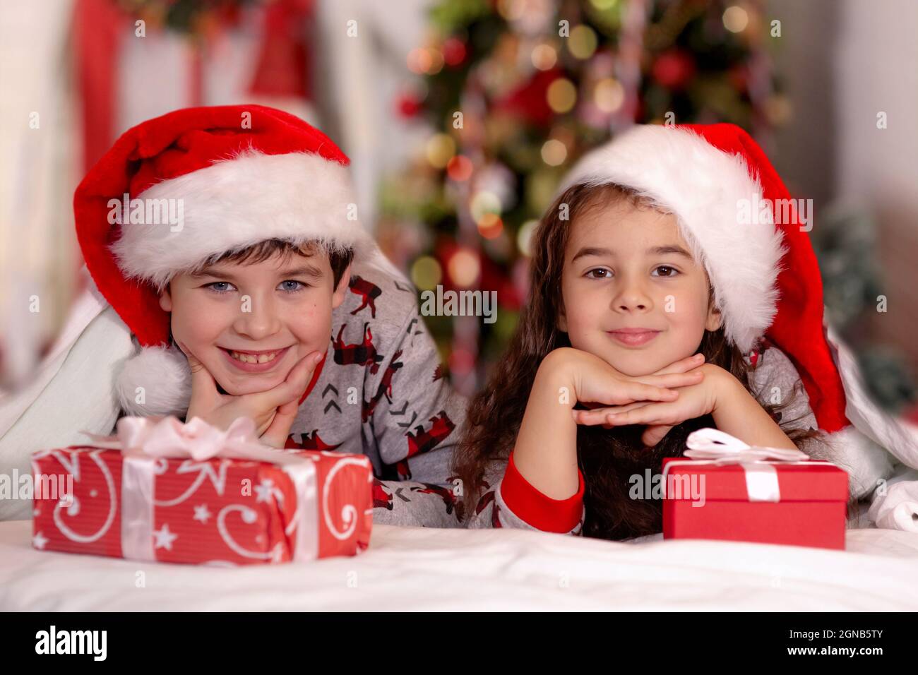 Two cute children, a girl and a boy, in santa claus hats, cuddle on ...