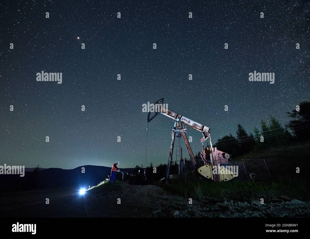 Oilman working the night shift in oil well. Worker checking operating ...