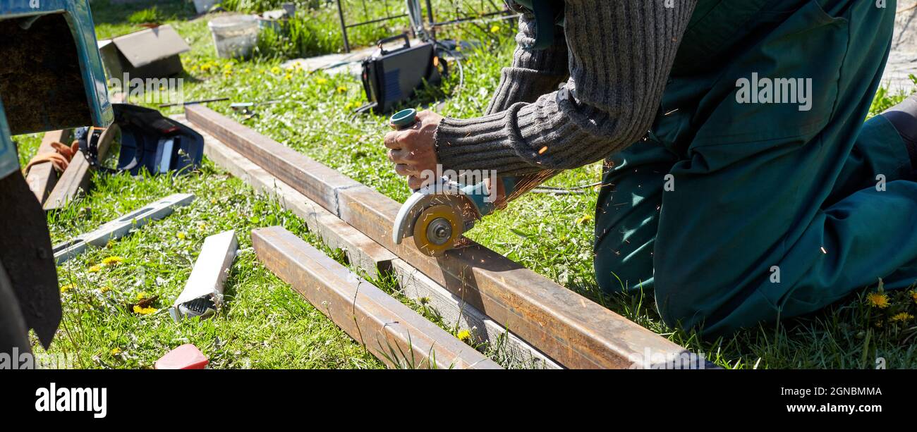 Man grinds a metal product with angle grinder outdoors. Metal ...