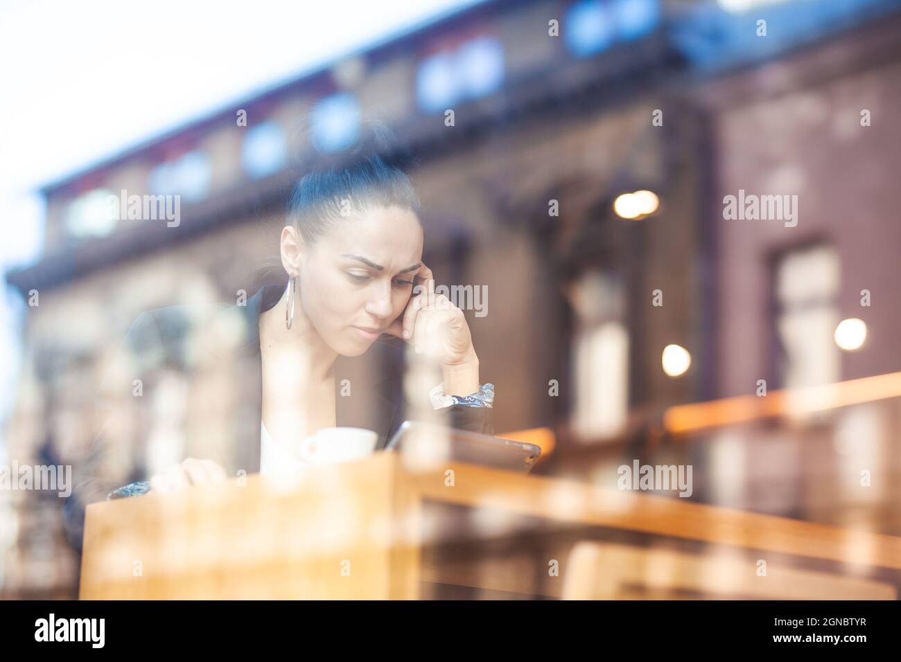 Businesswoman at a cafe, having coffee and looking at tablet. Window ...