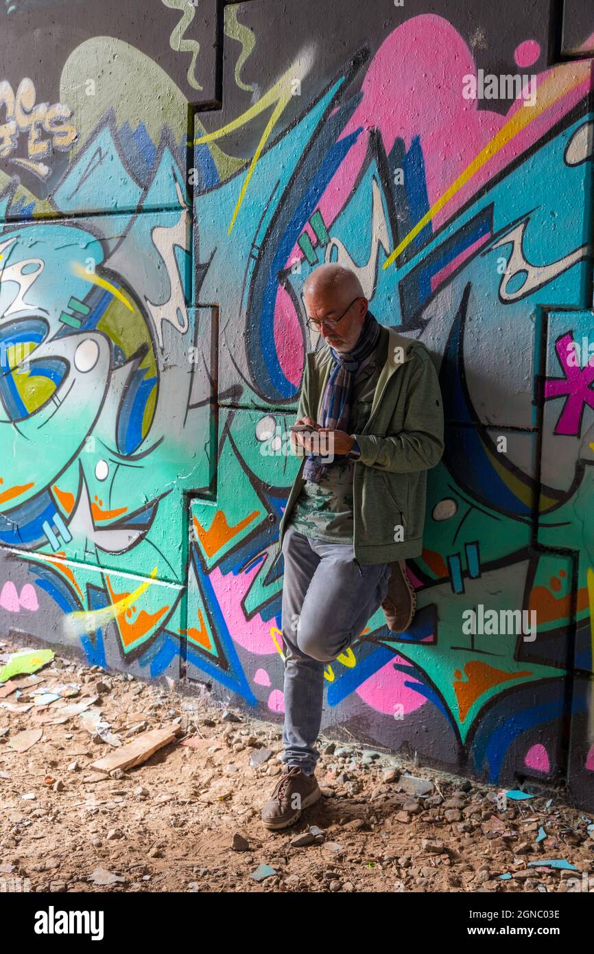 a wall full with graffiti and a man busy with his cellphone Stock Photo ...