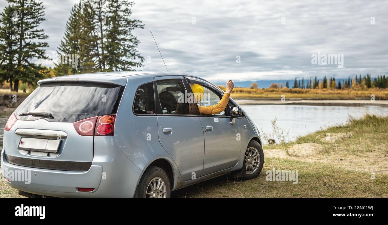 Man in a car next to river and forest, stretching his hand up of the ...