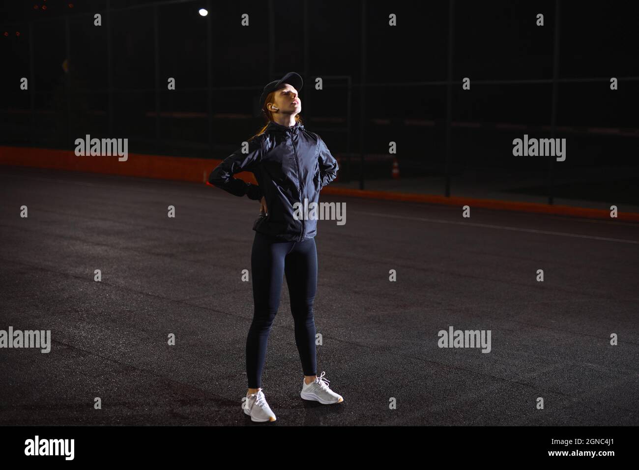 Side view of young female in sportive wear and cap walking, having rest ...