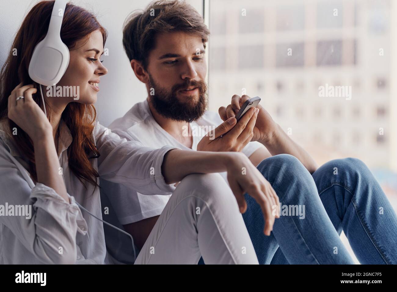 a young couple sit near the window with headphones together apartments ...