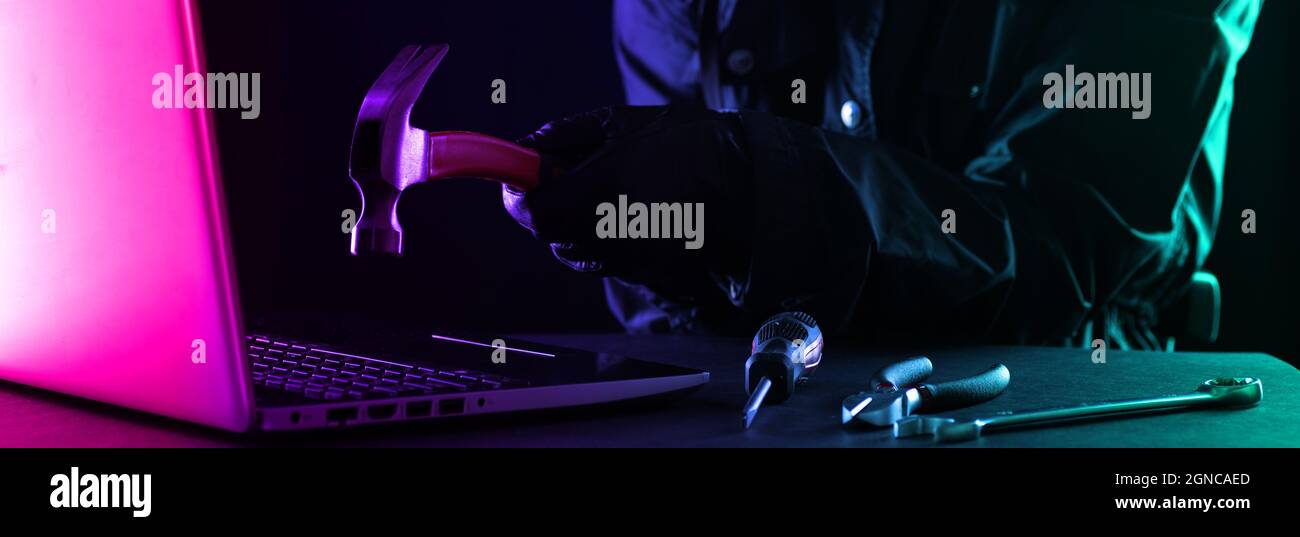 Criminal hacker in a hood in black clothes and balaclava destroys a ...