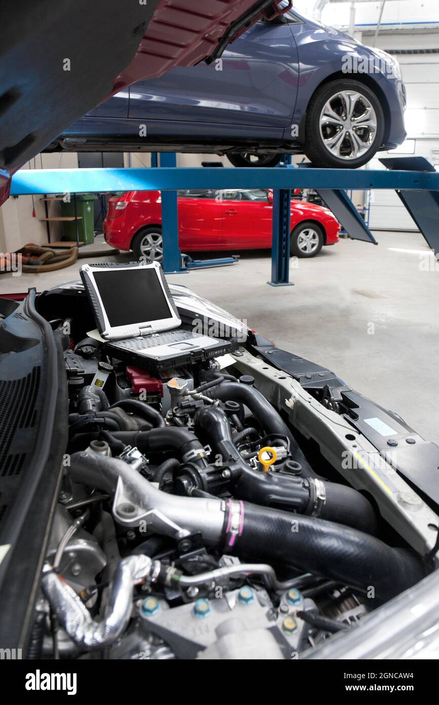 Car in a workshop and a computer running diagnostics on the engine ...