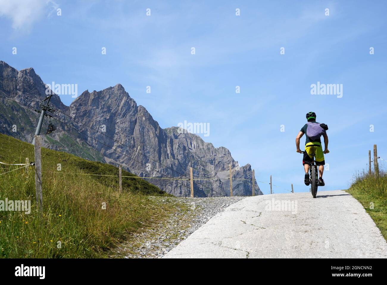 Man on a bicycle on a hilltop in rear view. There are Alp mountains on ...