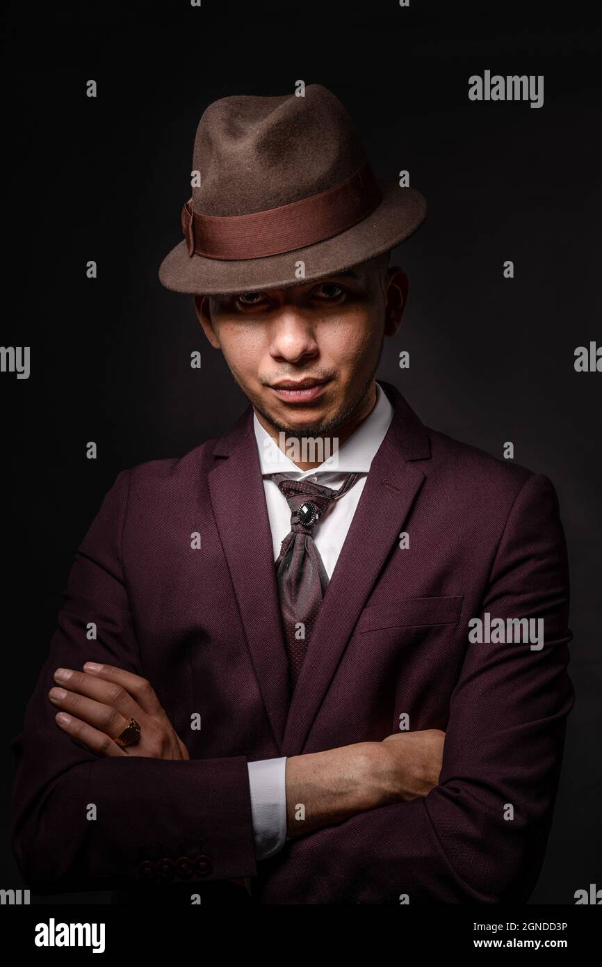 Caucasian man in suit hiding face behind his hat on dark background ...