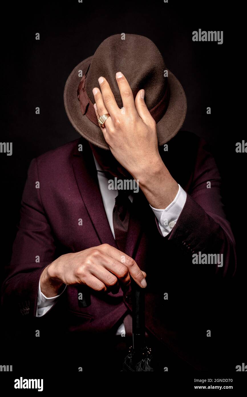 Caucasian man in suit hiding face behind his hat on dark background ...