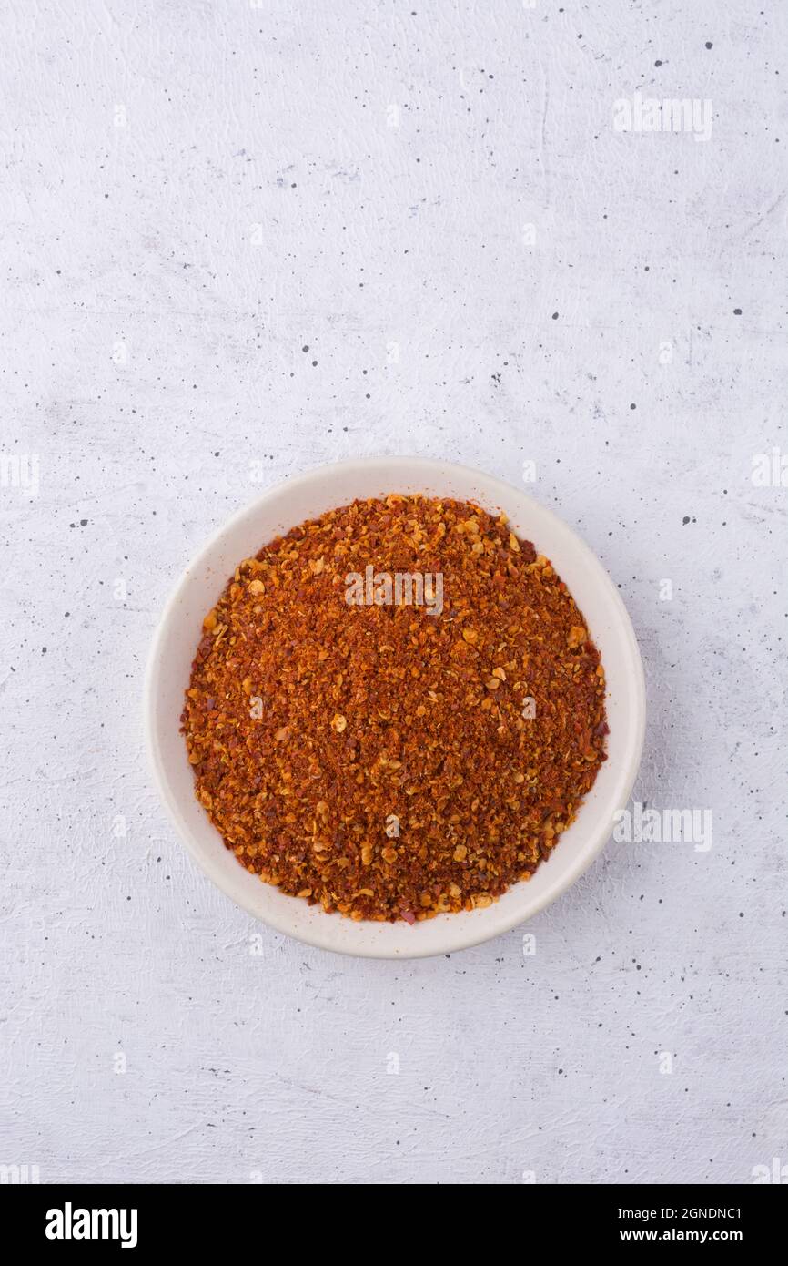 ground dried red chilli, spicy pepper powder on a small plate, closeup ...